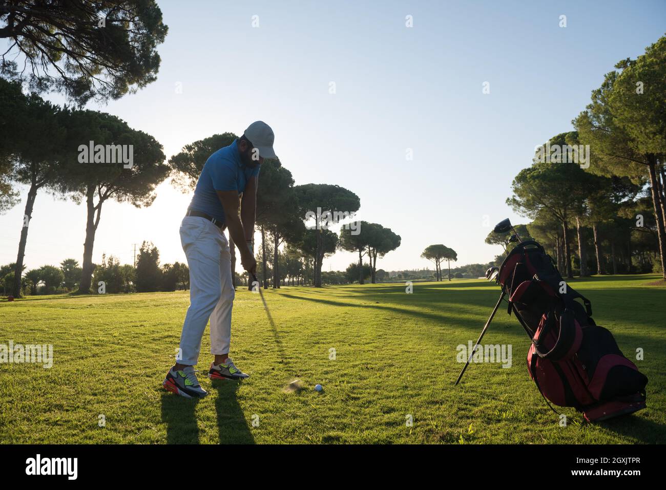 handsome sporty man, golf player hitting shot with club on course at ...