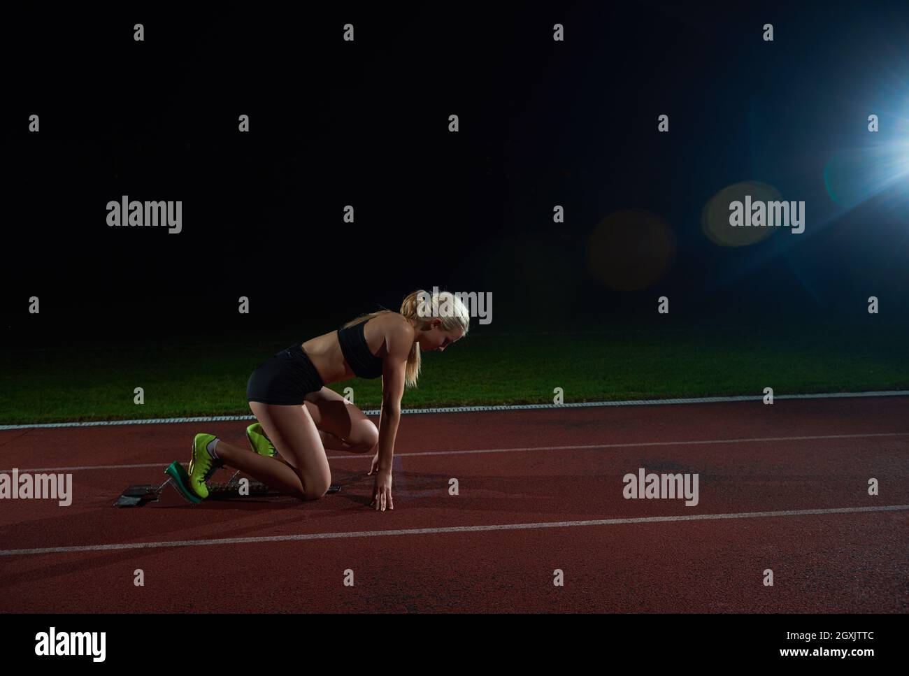 woman sprinter leaving starting blocks on the athletic track. Side view ...