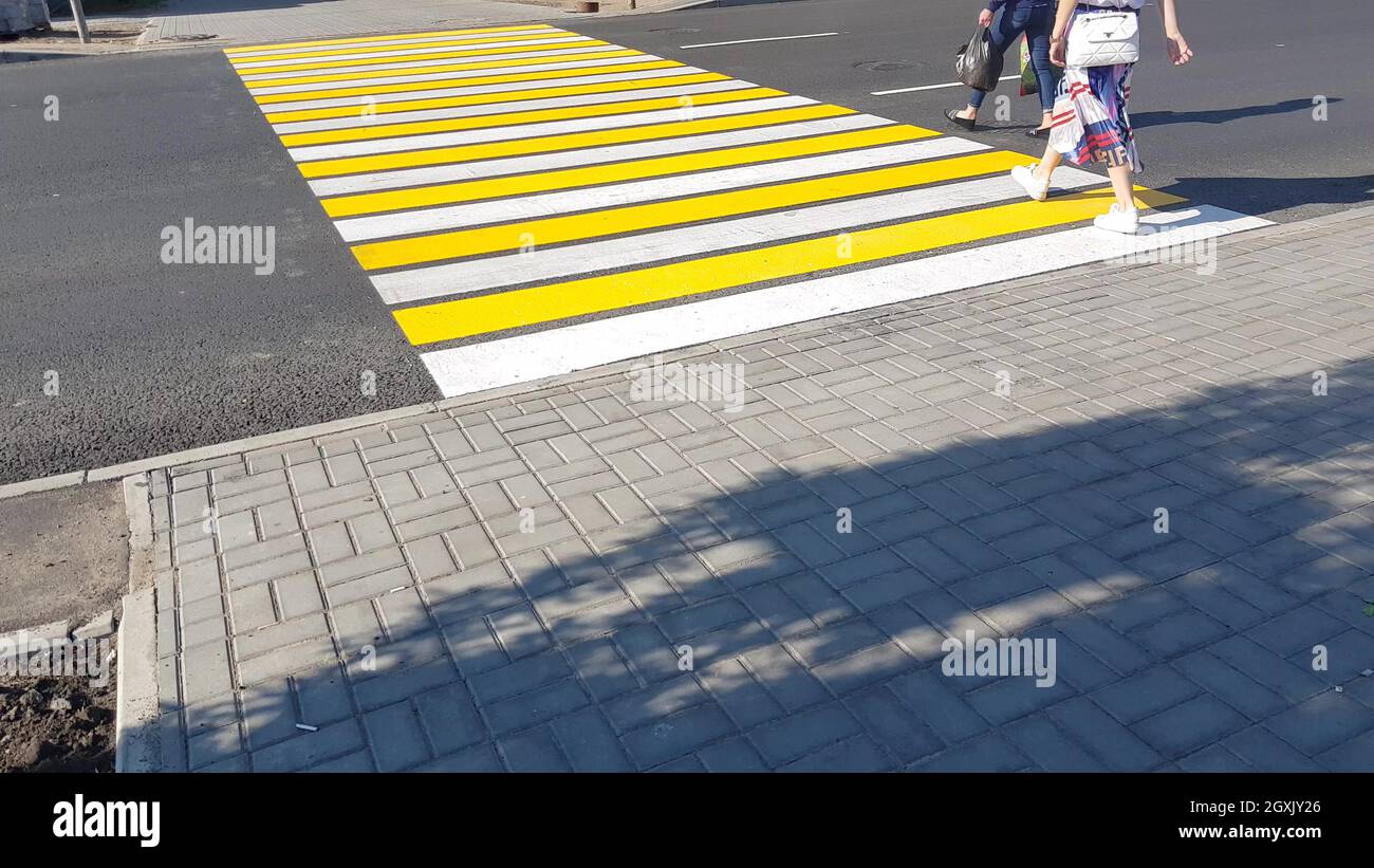 two pedestrians crossing the road on a new yellow-white marking of a ...