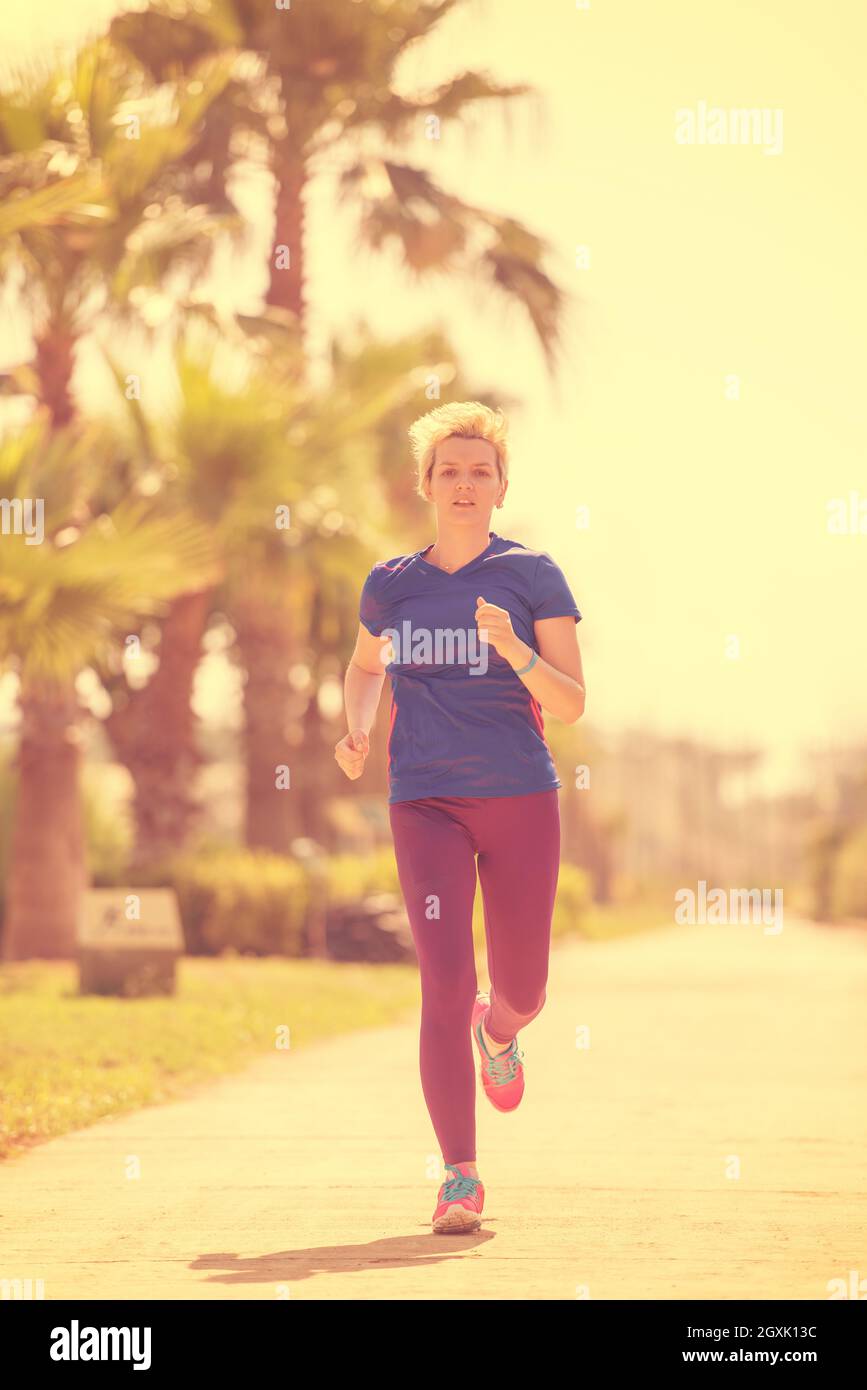 young sporty female runner training for marathon running at beautiful tropical park in the sunny ...