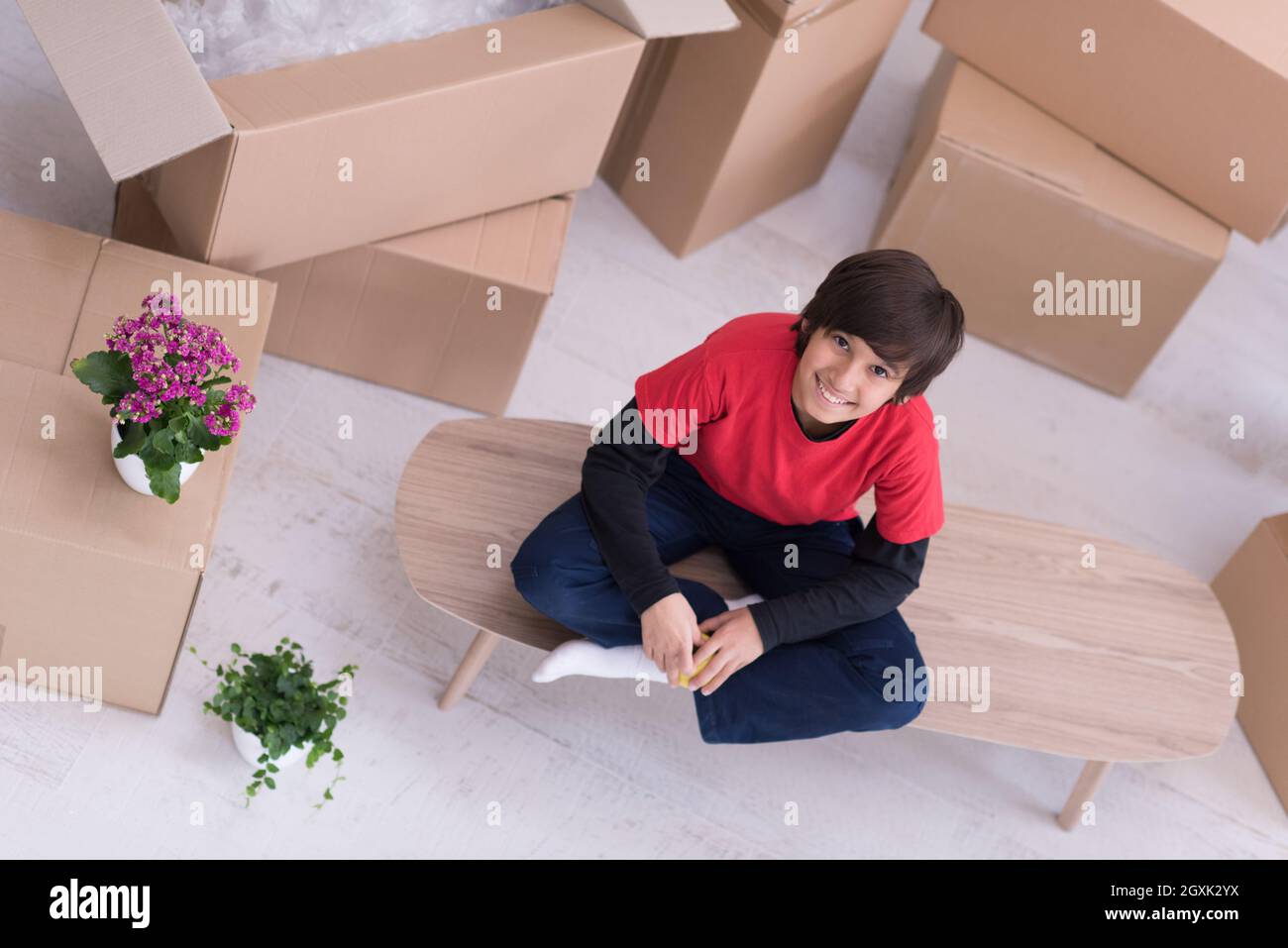 happy little boy sitting on the table with cardboard boxes around him ...