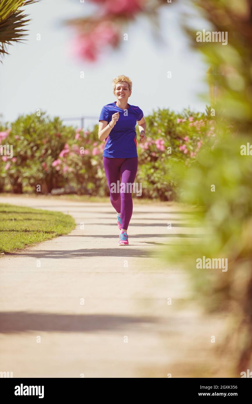 young sporty female runner training for marathon running at beautiful tropical park in the sunny ...