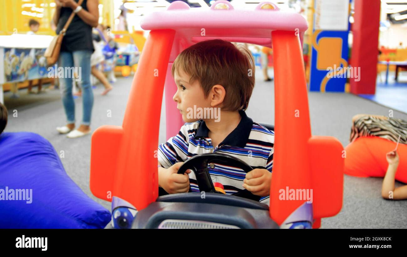 Portrait of smiling boy driving toy car in playing room at shopping ...