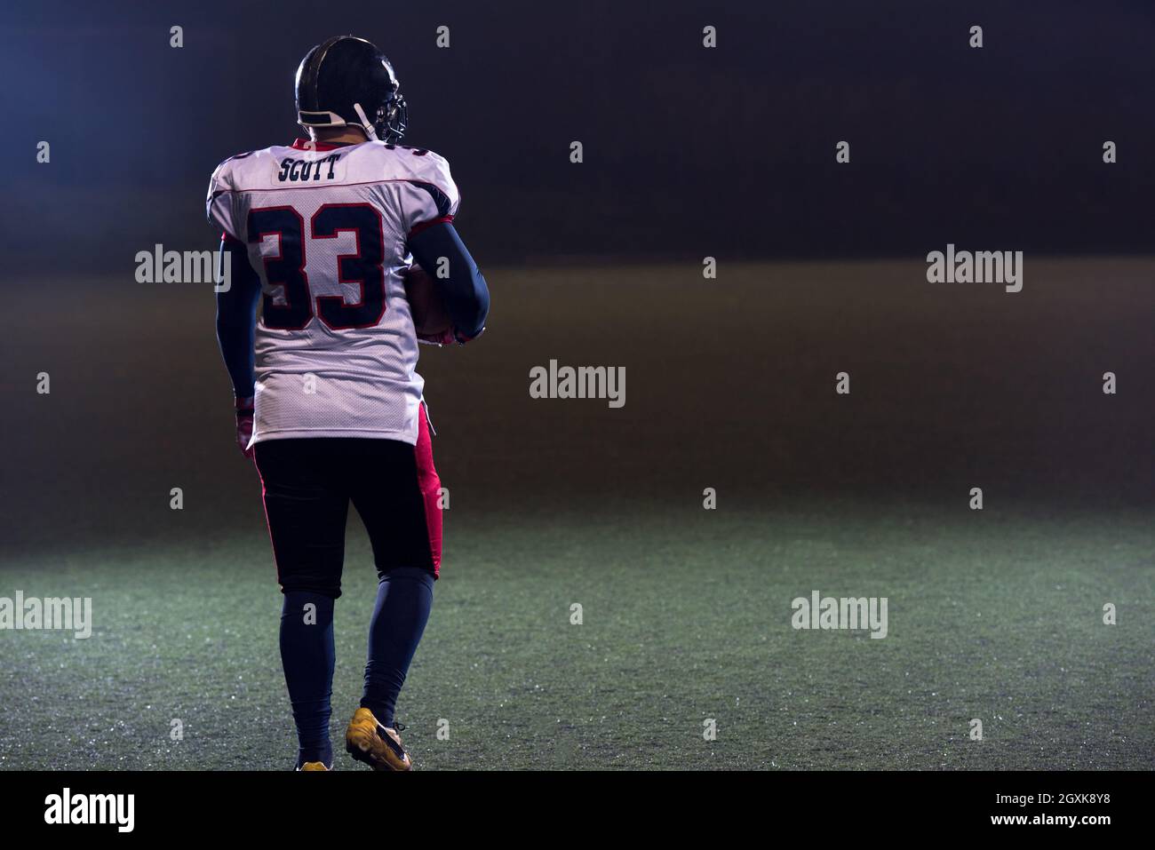 rear view of young confident American football player on field at night ...