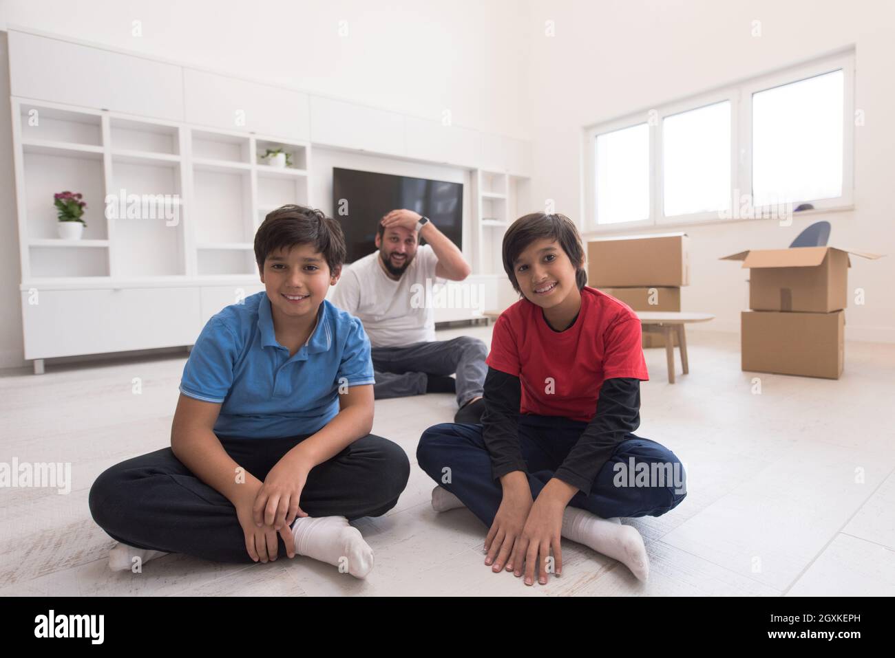 portrait of happy young boys with their dad sitting on the floor in a ...