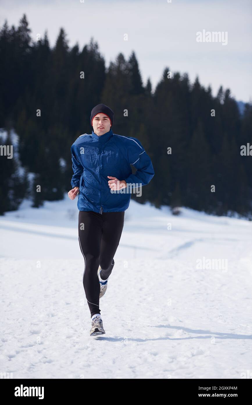 young man jogging on snow in forest, bautiful sunny winter day ...