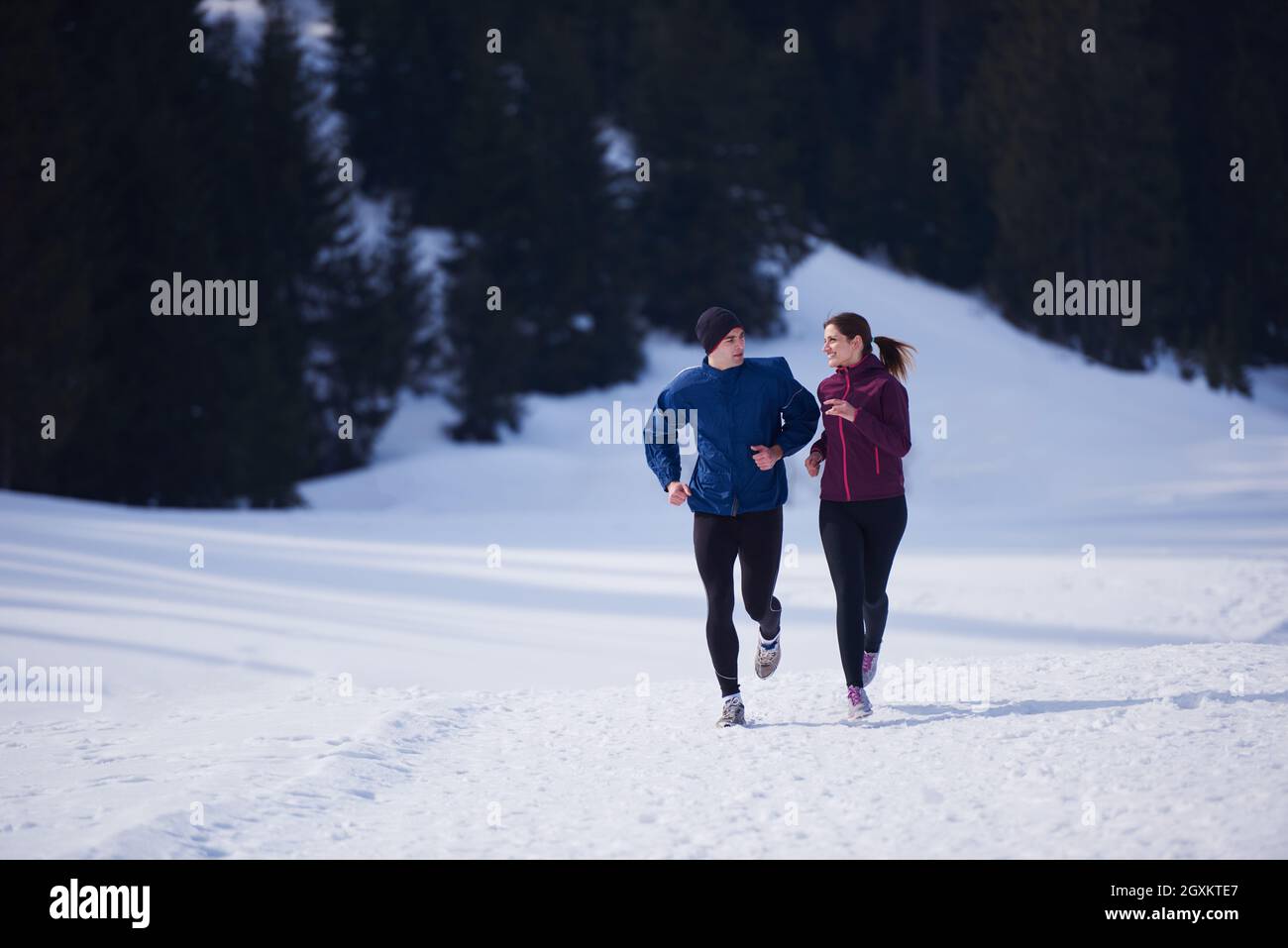 healthy young couple jogging outside on snow in forest. athlete running ...