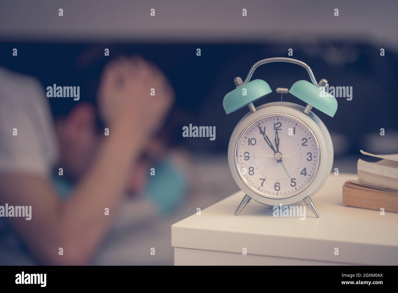 White alarm clock on the bedside table. Young tries to sleep in the ...