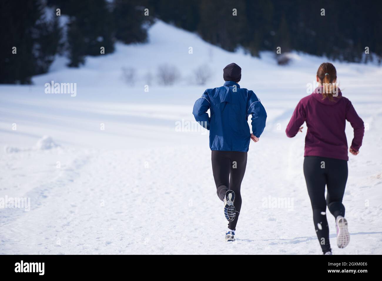 healthy young couple jogging outside on snow in forest. athlete running ...