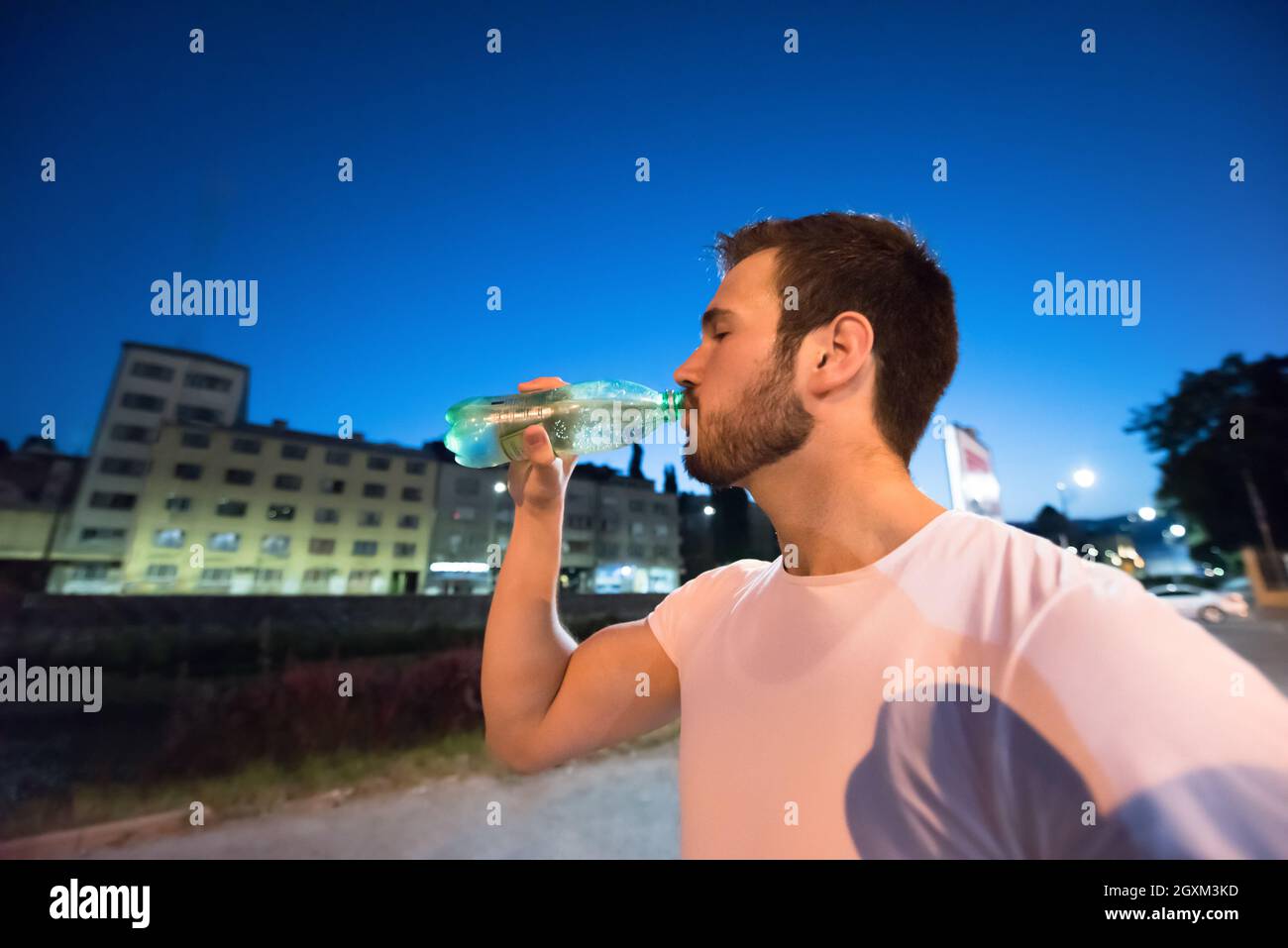 young athletic man drinking water after a night running session in the ...