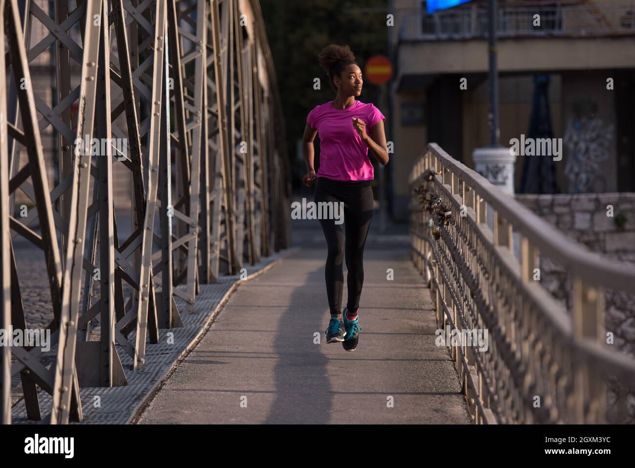 Young sporty african american woman running on sidewalk across the ...