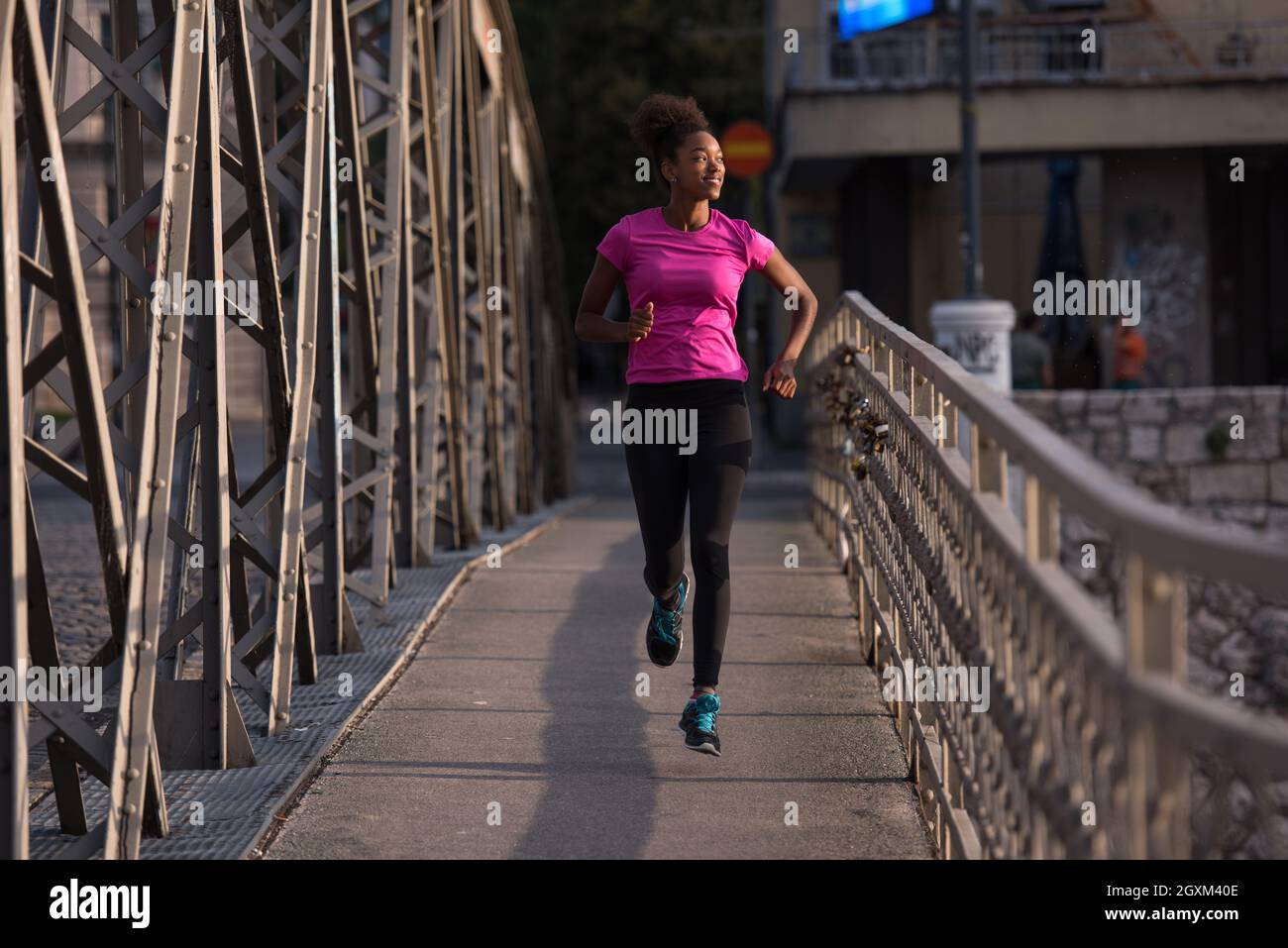 Young sporty african american woman running on sidewalk across the ...
