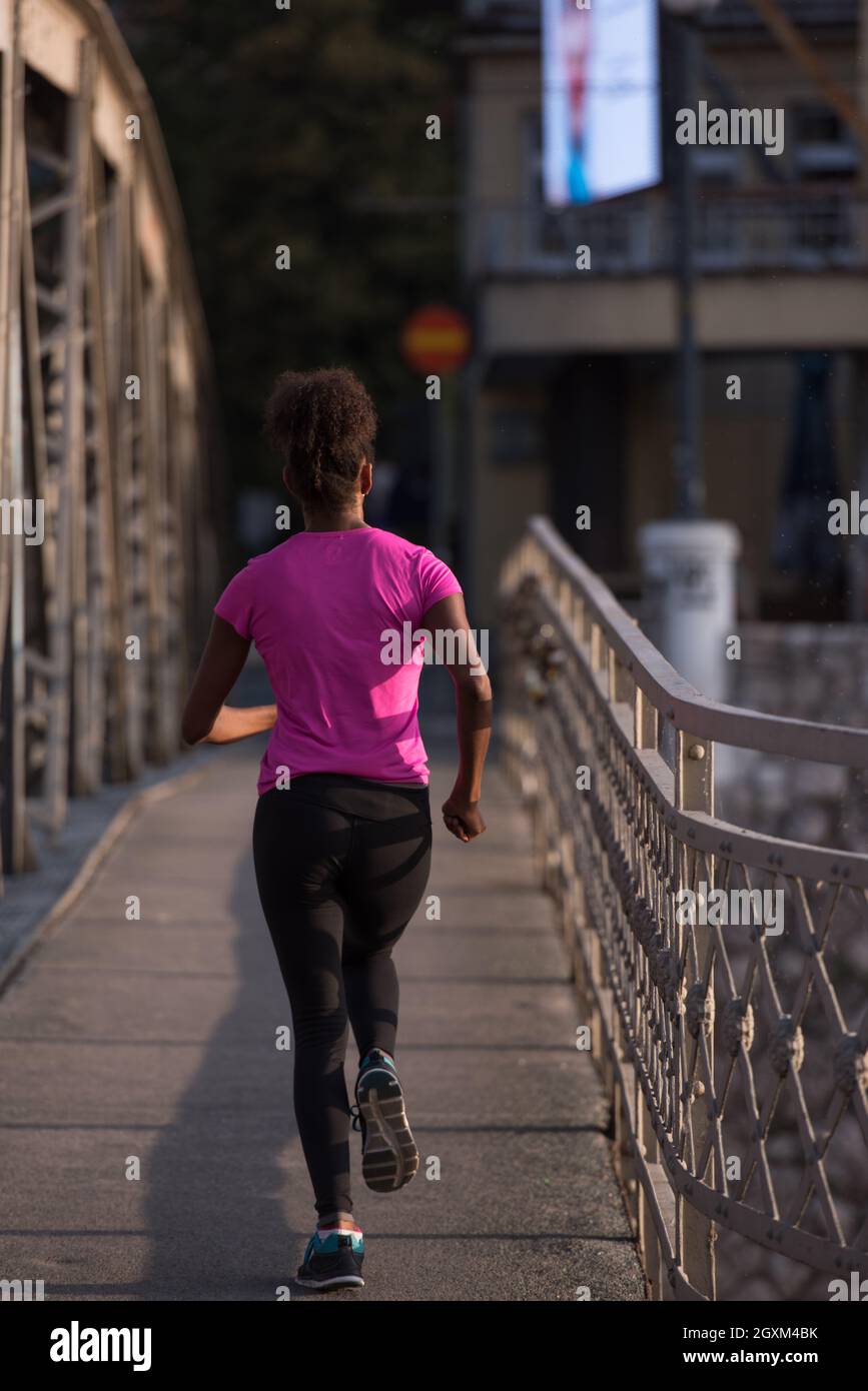 Young sporty african american woman running on sidewalk across the ...