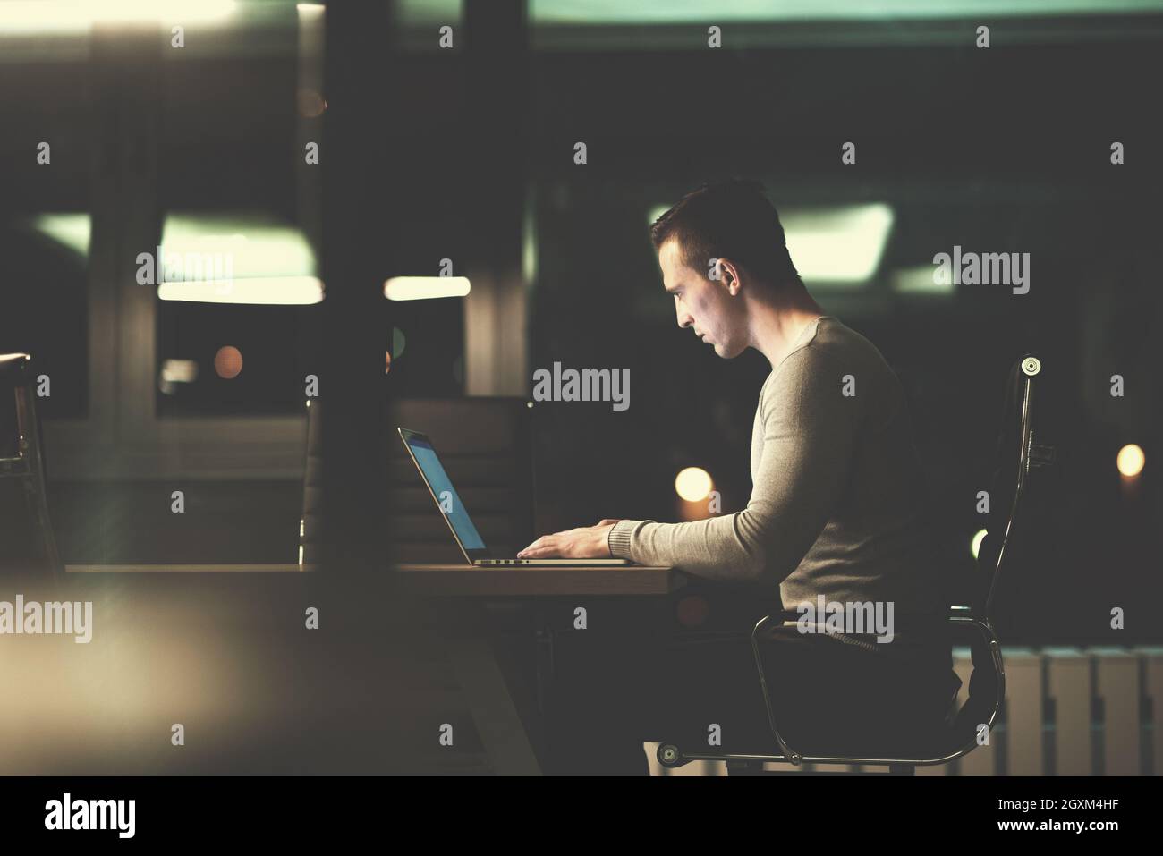 Young man working on laptop at night in dark office. The designer works ...