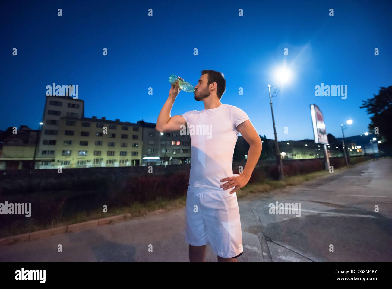 young athletic man drinking water after a night running session in the ...