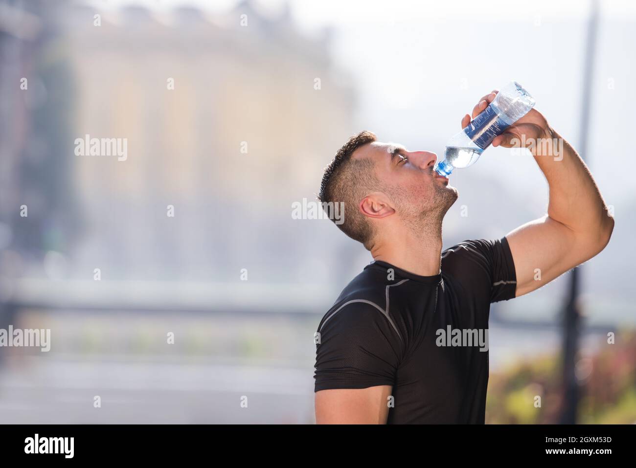 Athlete man drinking water from a bottle after jogging in the city on a ...