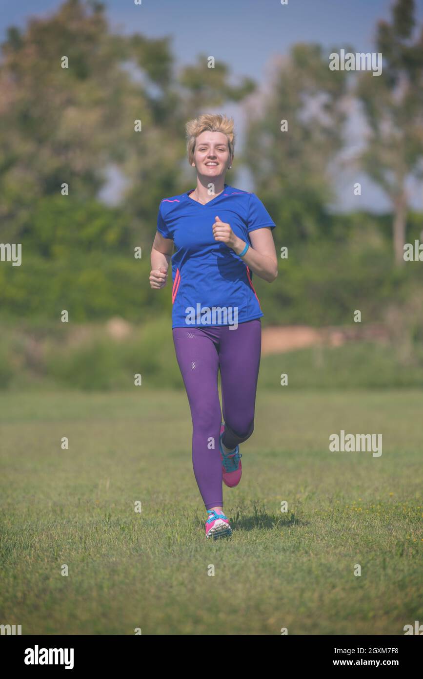 young sporty female runner training for marathon running at beautiful tropical park in the sunny ...