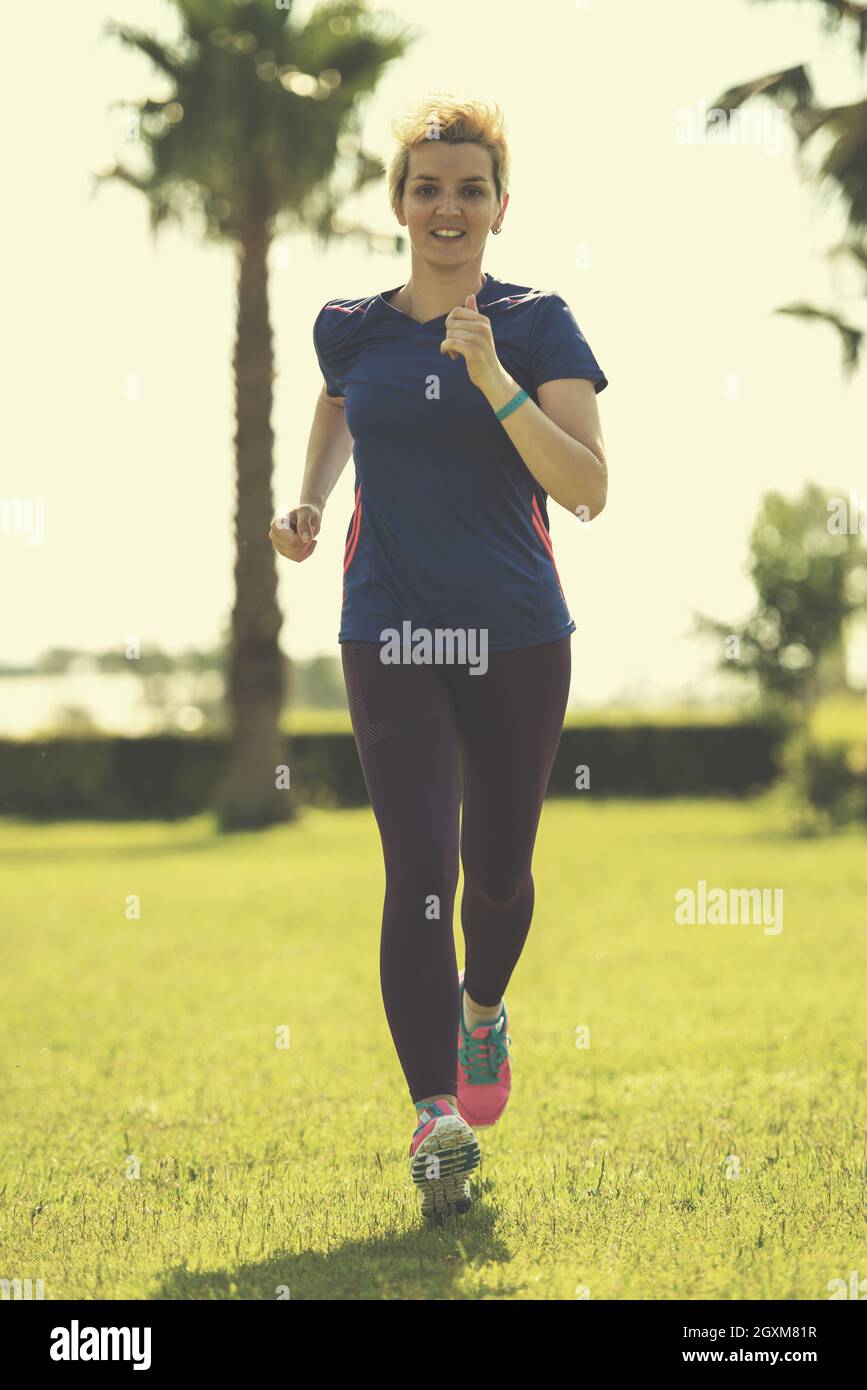 young sporty female runner training for marathon running at beautiful tropical park in the sunny ...