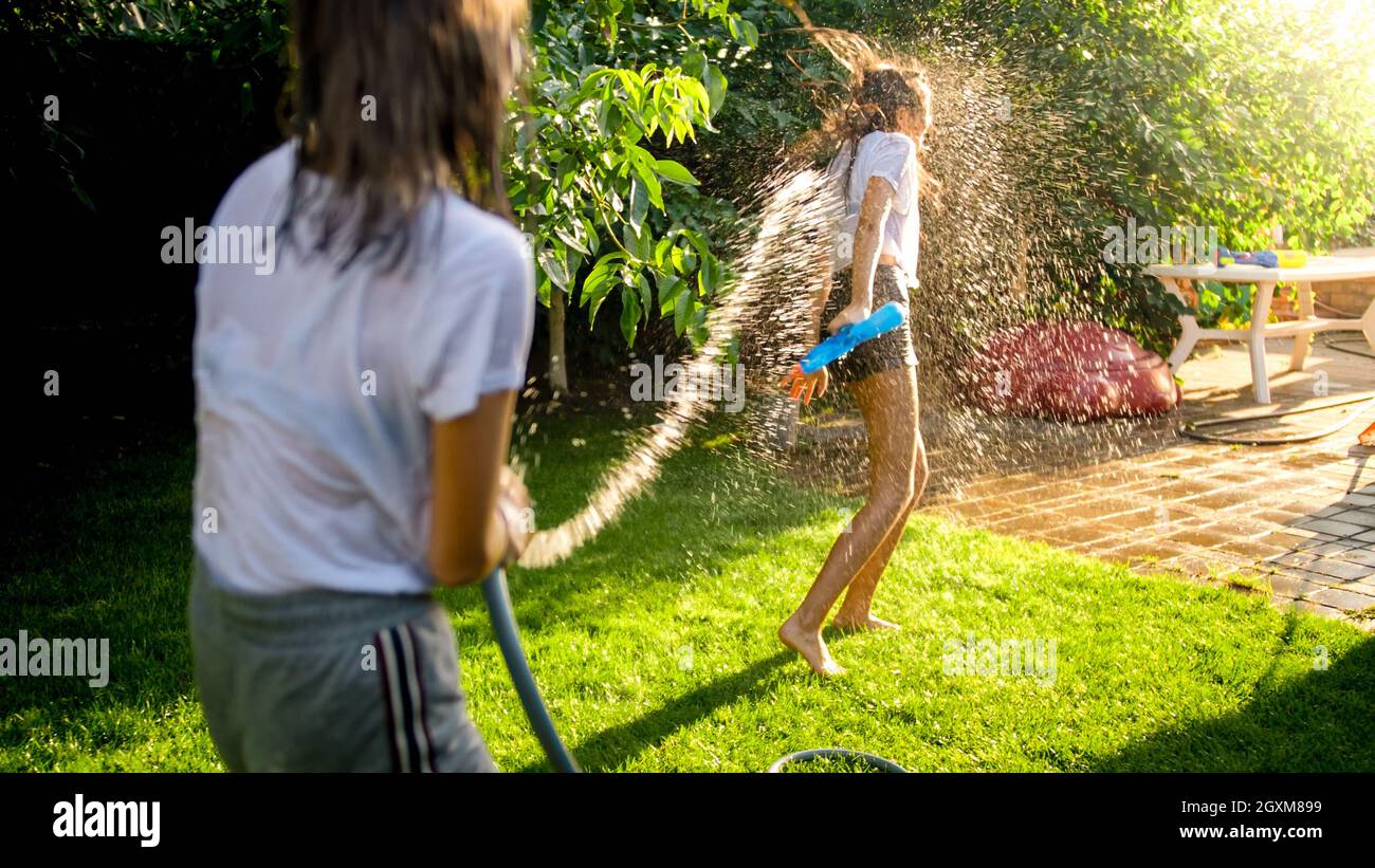 Two teenage girls playing water fight and splashing water from garden ...
