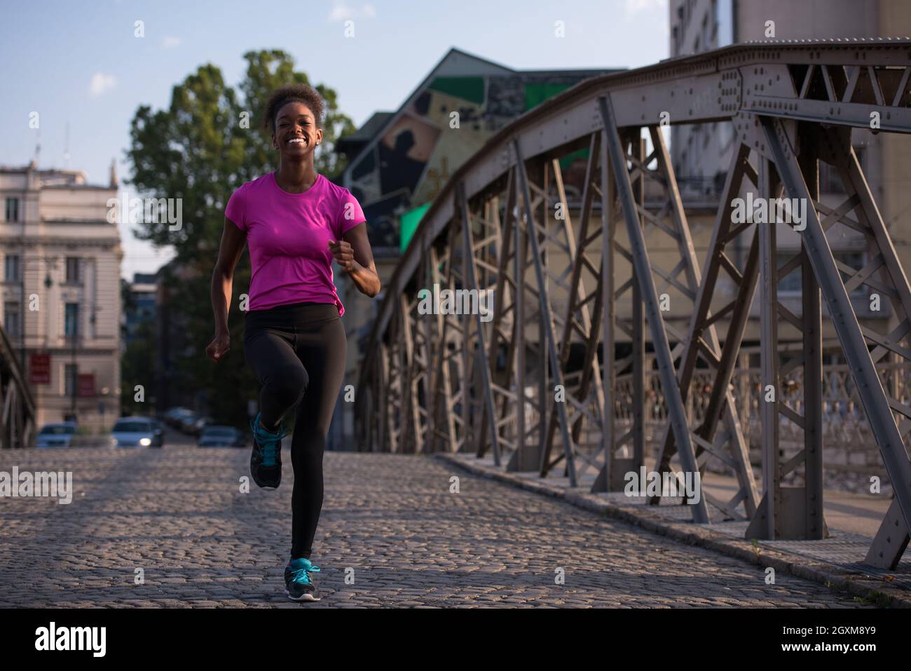 Young sporty african american woman running on sidewalk across the ...