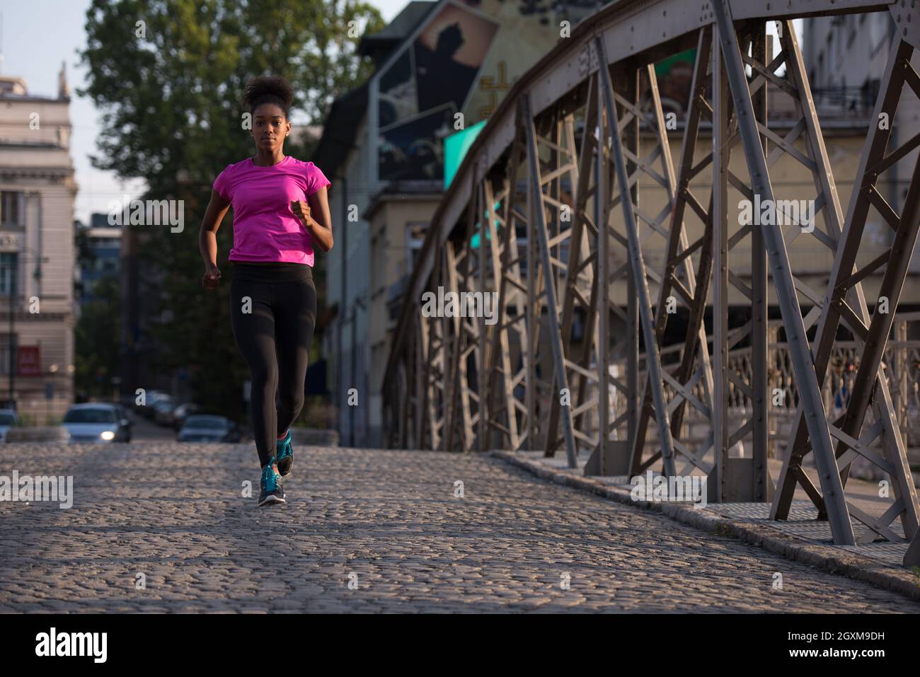 Young sporty african american woman running on sidewalk across the ...