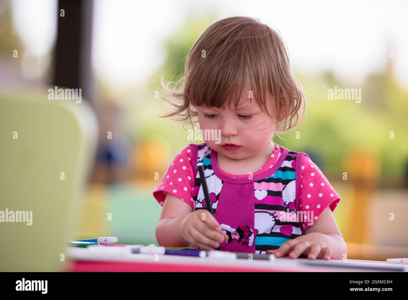 cute little girl cheerfully spending time using pencil crayons while ...