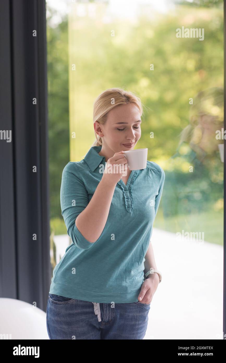 beautiful young woman drinking morning coffee by the window in her home ...