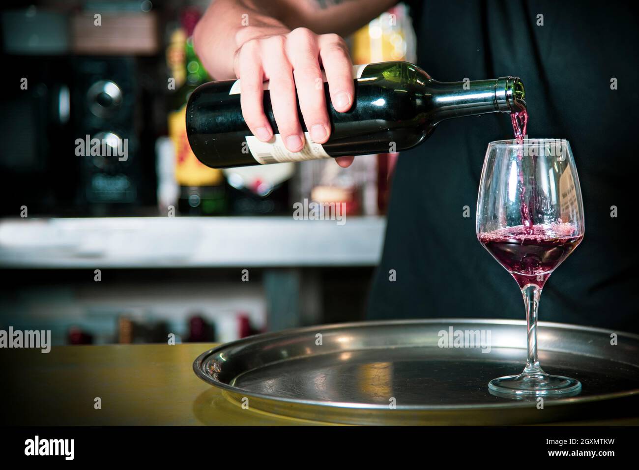 Waiter putting wine, in a glass on a typical metal tray, inside the bar ...