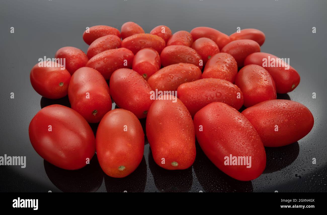 Plum tomatoes and cherry tomato composition on a dark glass background ...