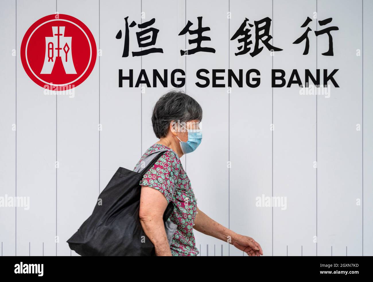 A woman wearing a face mask walks past the Hang Seng Bank branch and ...