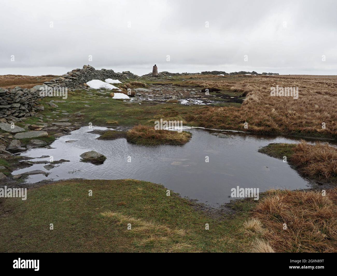 large puddle alongside dry stone wall and piles of melting snow ...