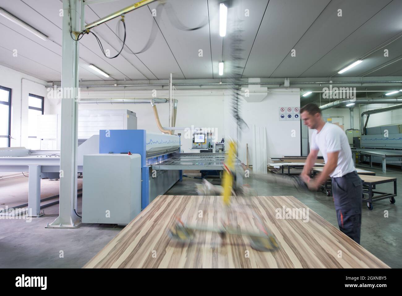 Young worker works in a factory for the production of wooden furniture ...