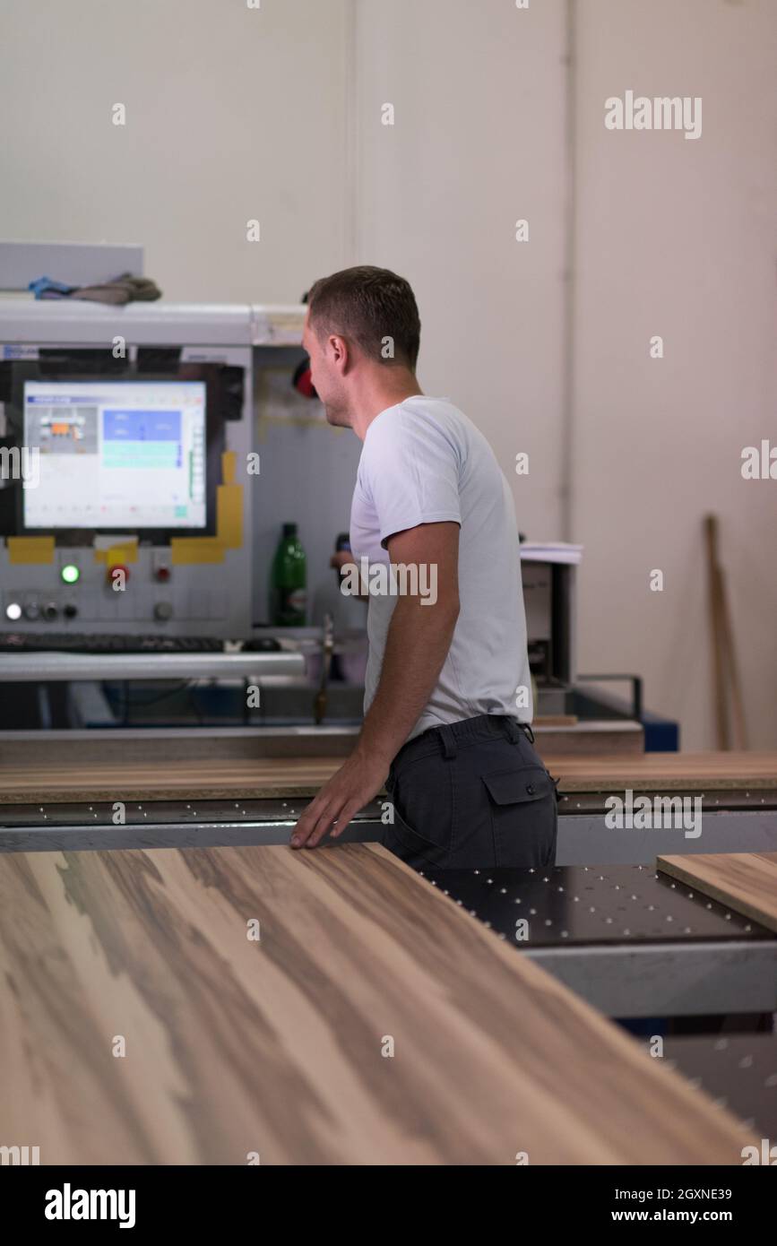Young worker works in a factory for the production of wooden furniture ...