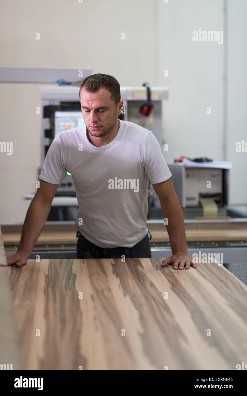Young worker works in a factory for the production of wooden furniture ...