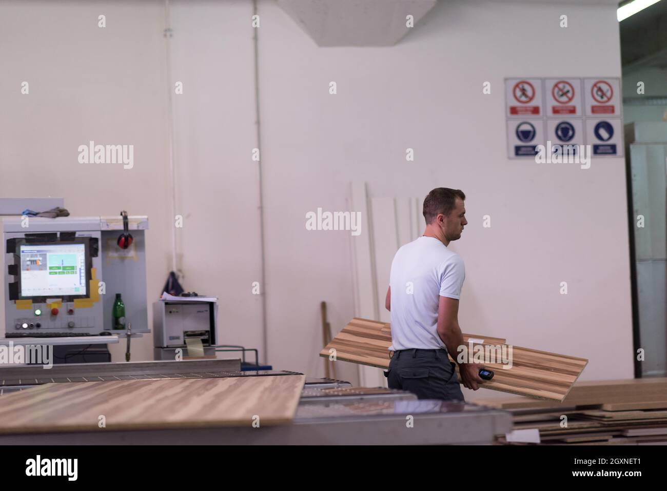 Young worker works in a factory for the production of wooden furniture ...