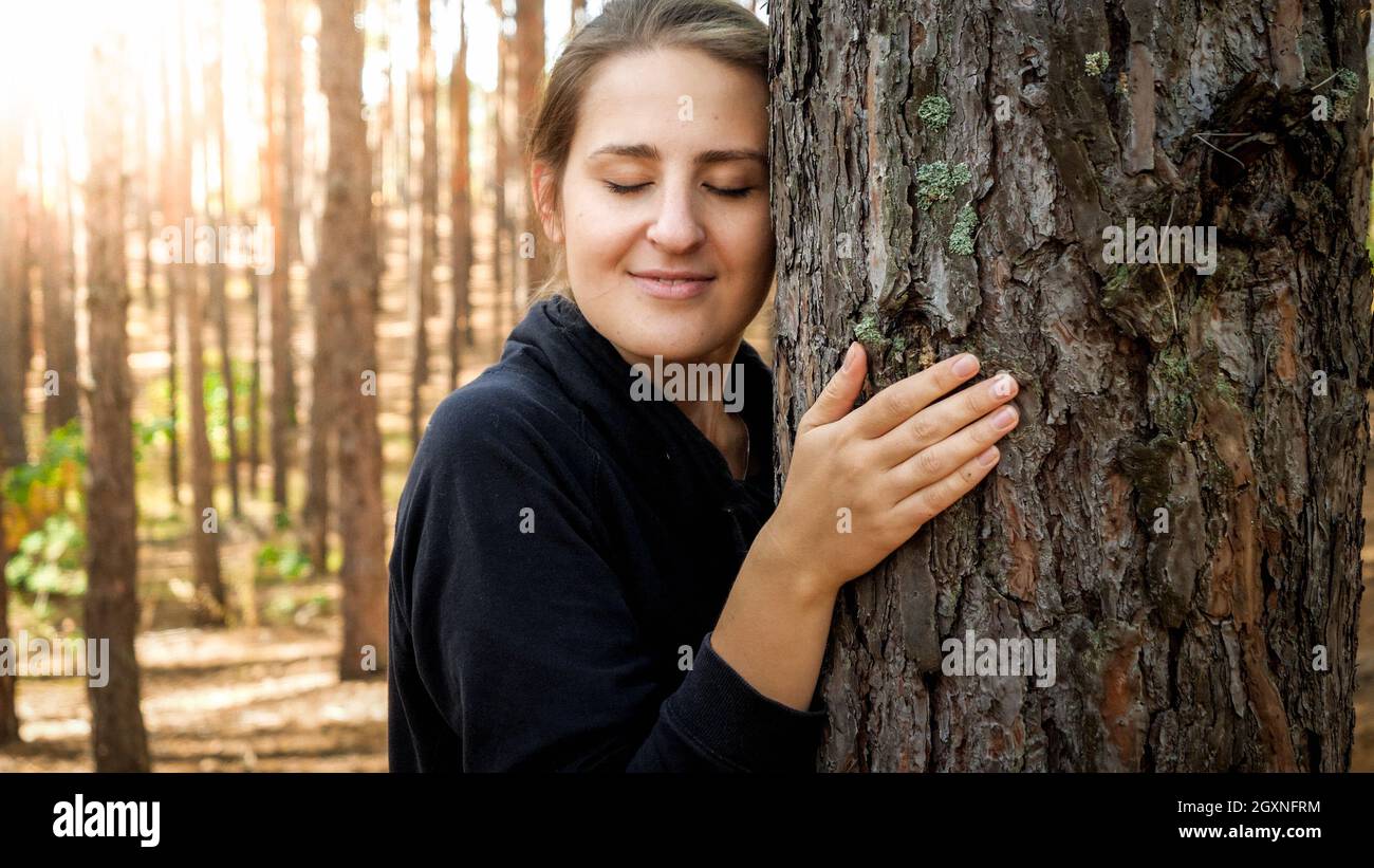 Portrait of beautiful young woman leaning and touching big old tree in ...