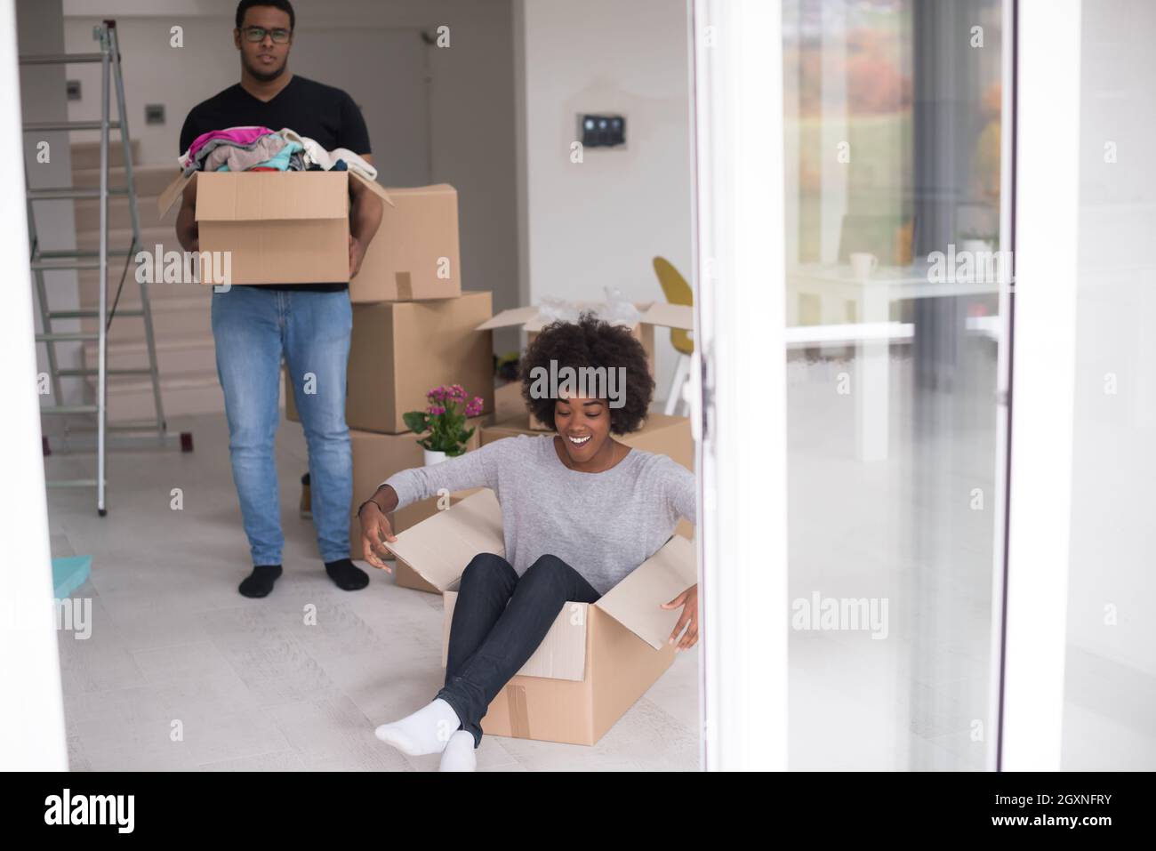 African American couple sitting in a box playing with packing material ...