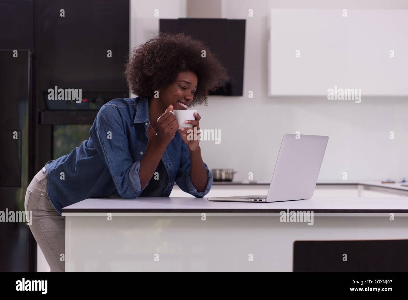 Young smiling black woman using computer and drinking coffee in modern ...