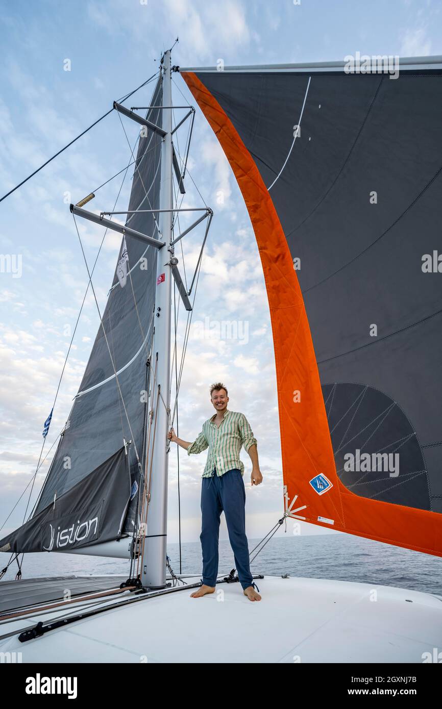 Young man standing between the sails of a sailing catamaran, mast with ...