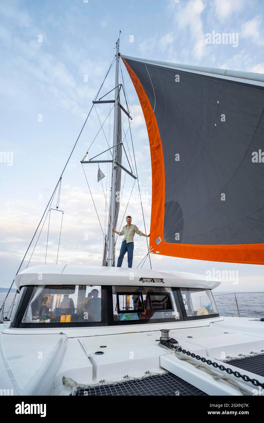 Young man standing between the sails of a sailing catamaran, mast with ...