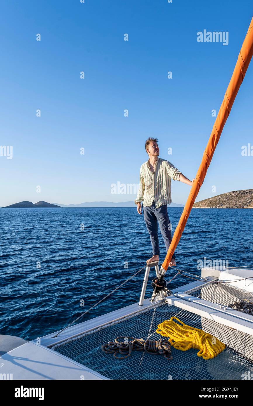 Young man standing by the furled headsail, ropes in the net, sailing ...