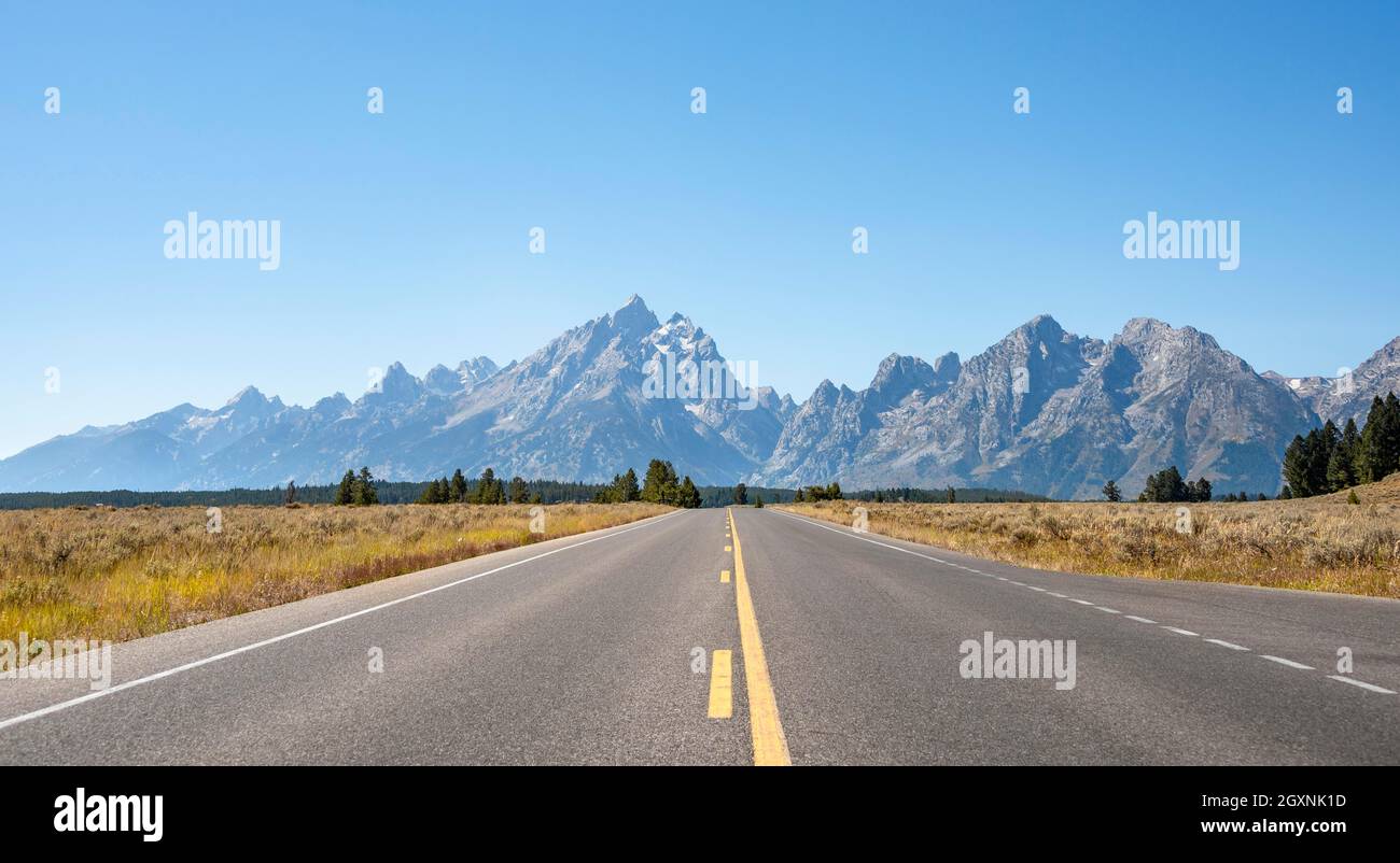 Country road through autumn landscape, rugged mountain peaks behind ...
