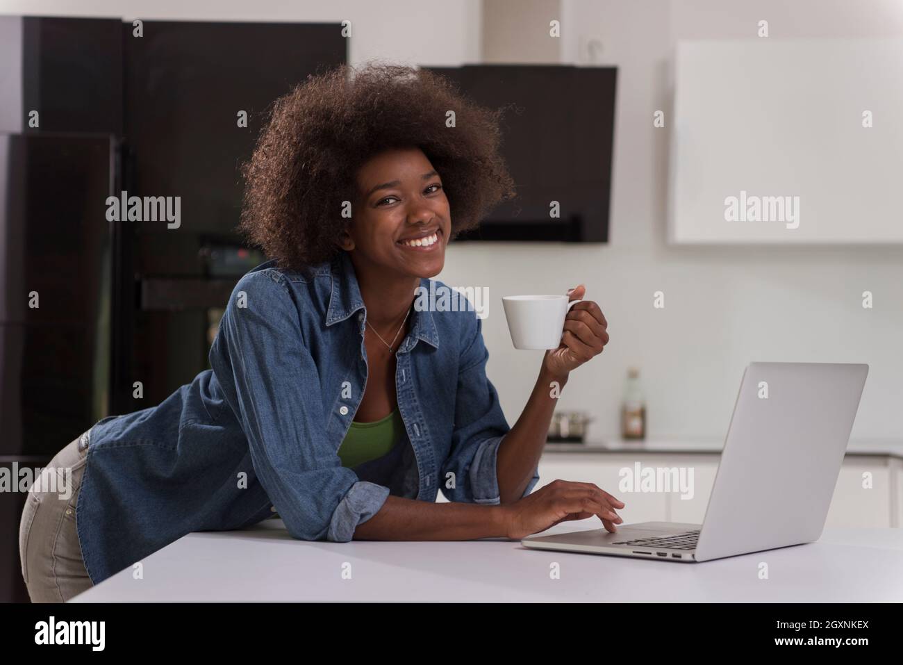 Young smiling black woman using computer and drinking coffee in modern ...