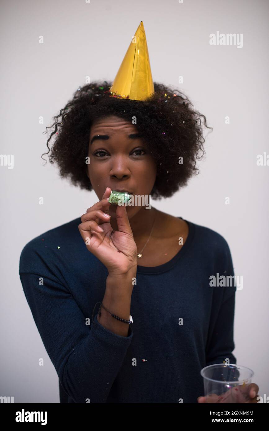 portrait of a young beautiful black woman in party hat blowing in ...
