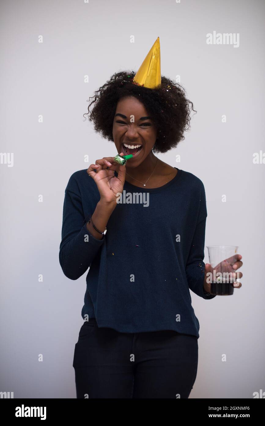 portrait of a young beautiful black woman in party hat blowing in ...