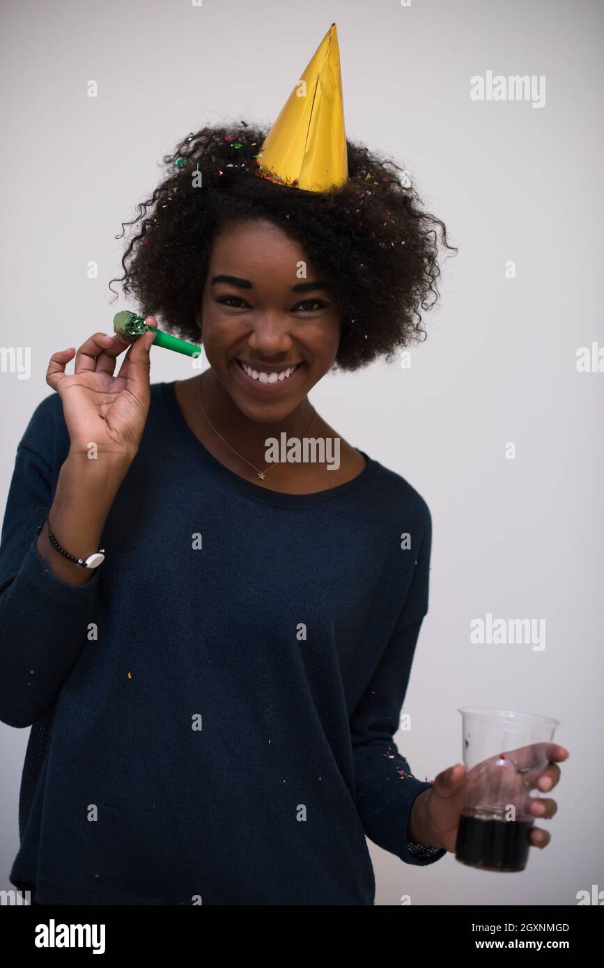 portrait of a young beautiful black woman in party hat blowing in ...