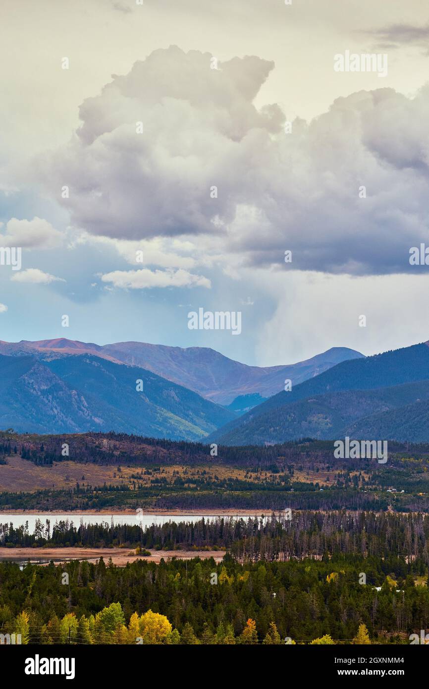 Vertical of mountains with rain clouds and water with pine trees ...