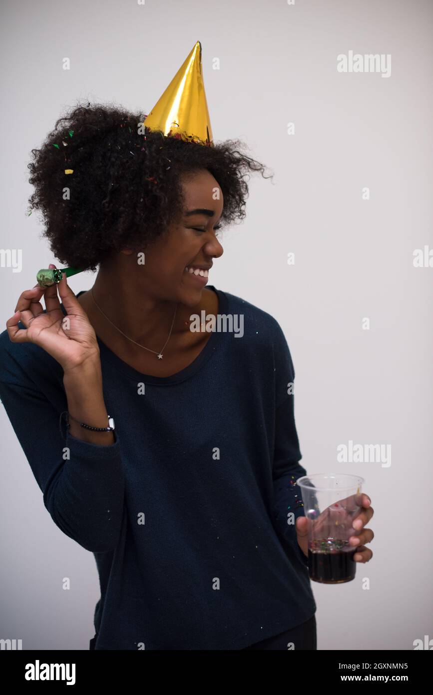 portrait of a young beautiful black woman in party hat blowing in ...
