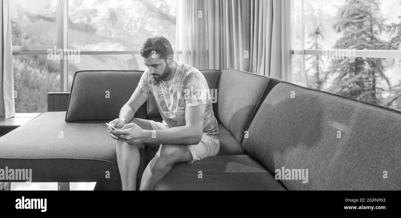 young man sitting on sofa and using a mobile phone near the window at ...