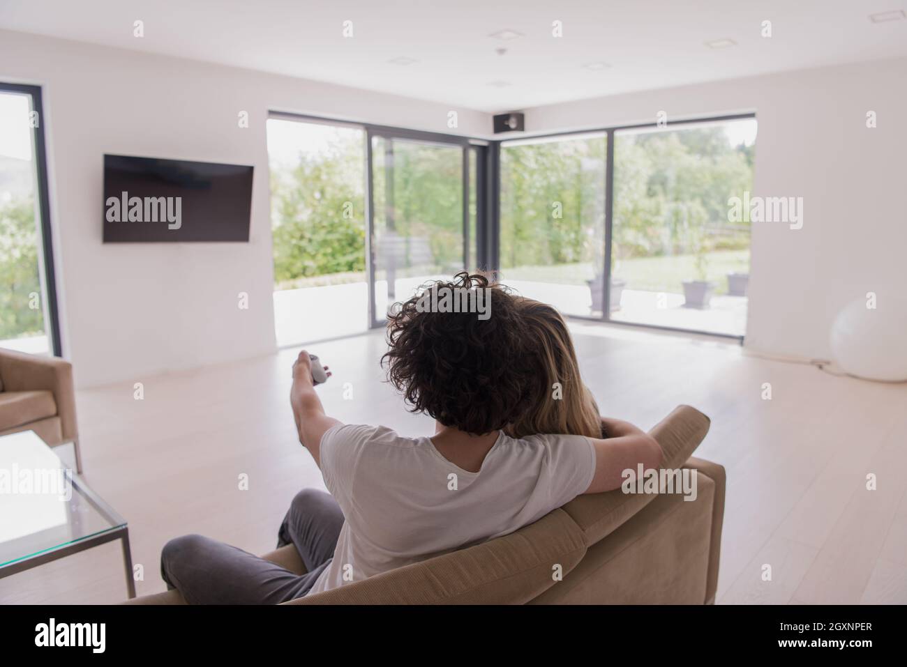 Rear view of couple watching television in living room their luxury ...